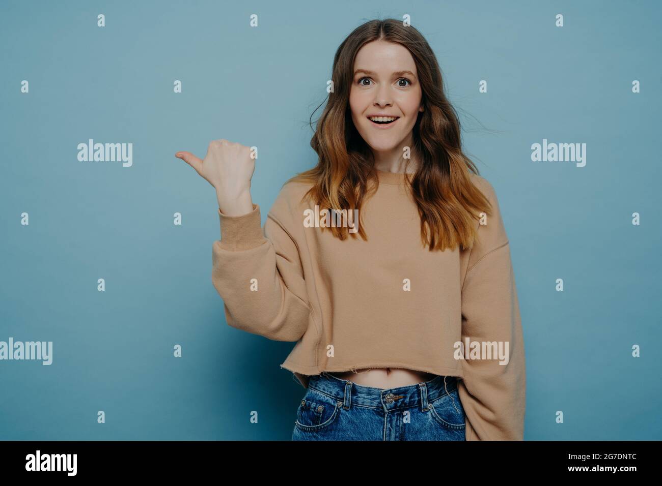 Excited young girl pointing finger somewhere posing over blue ...