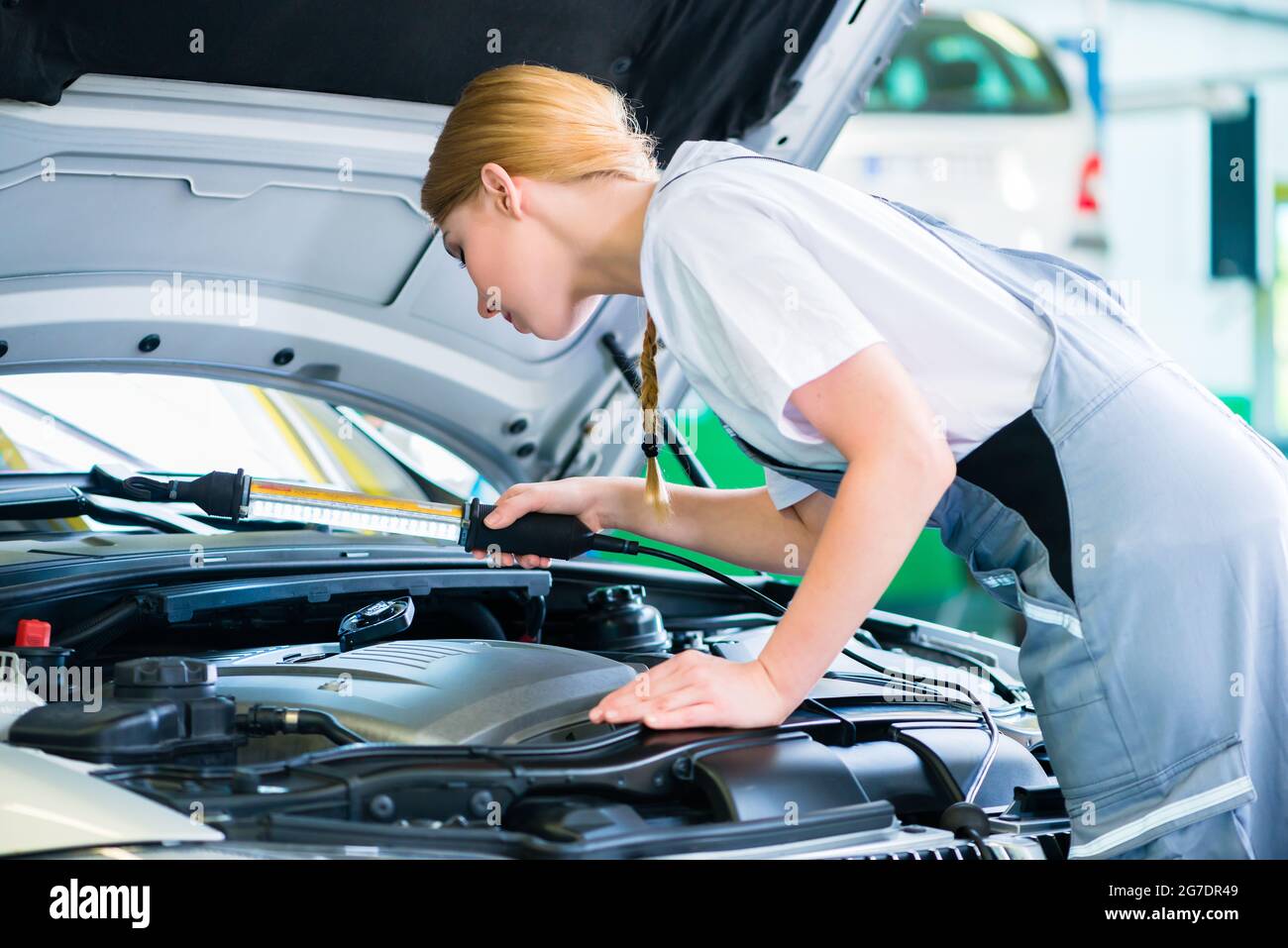 Female mechanic examine car engine with light in workshop Stock Photo ...
