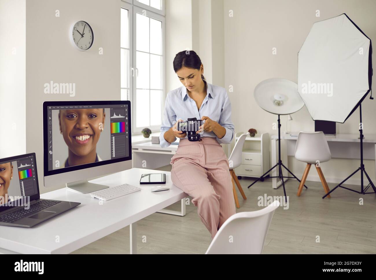 Photographer looking at photos on her camera while sitting on desk with ...