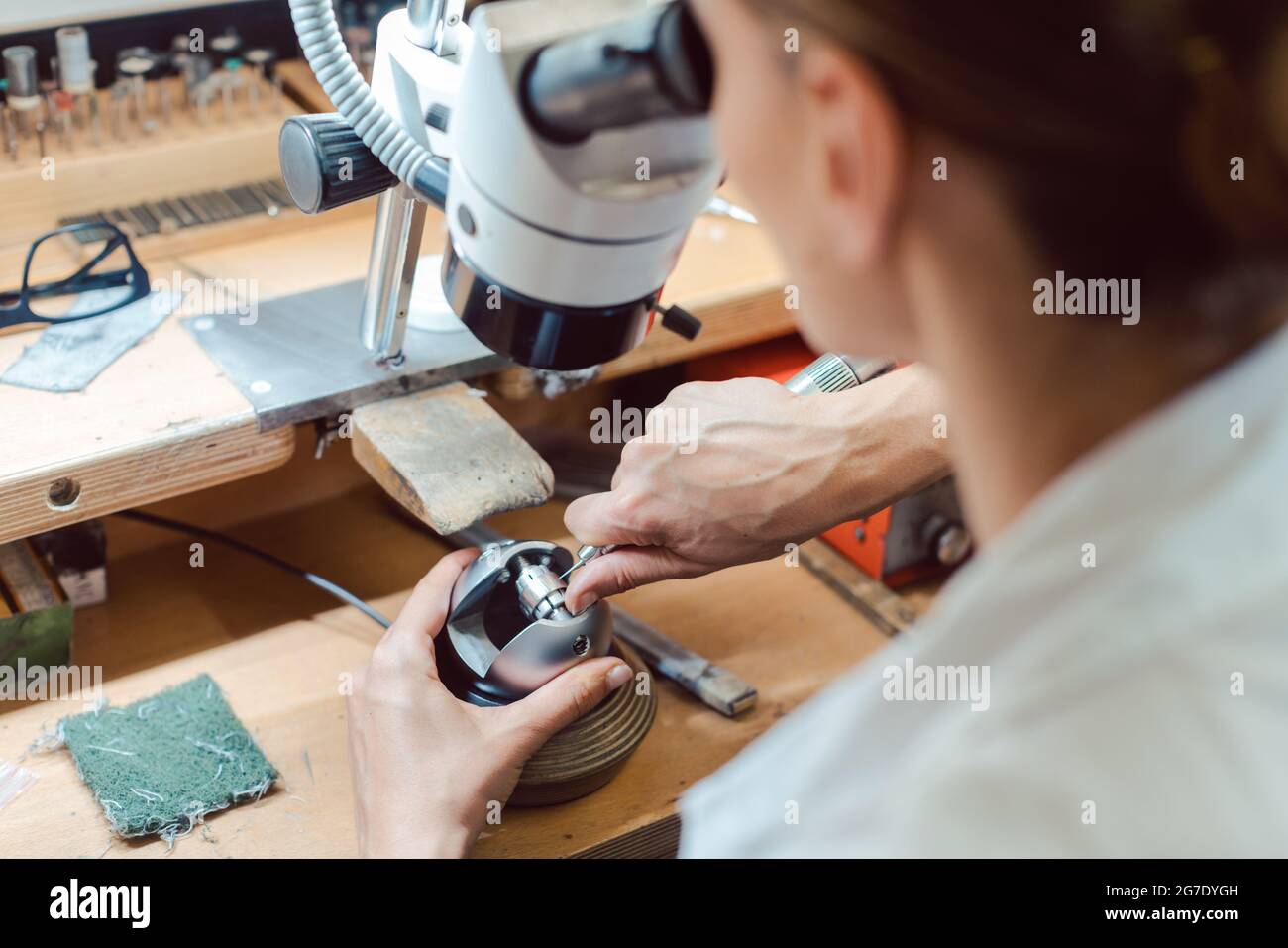 Diligent jeweler working on microscope at her workbench on some jewelry ...