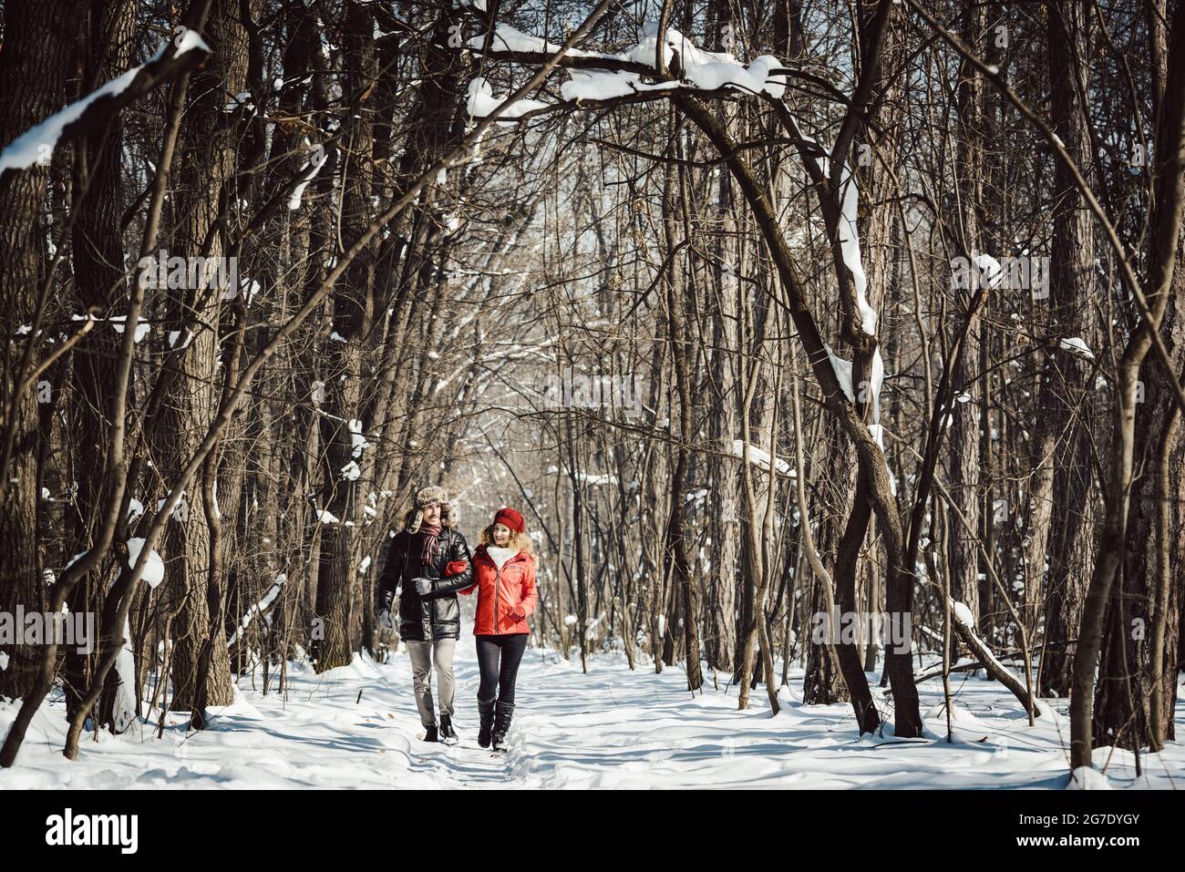 Couple having a winter walk on a chilly cold day in the woods down a ...