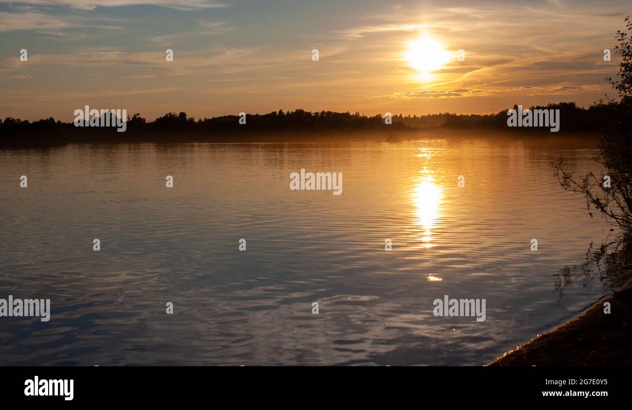 Colorful sunny sunset on a calm lake. The sun is reflected on the ...