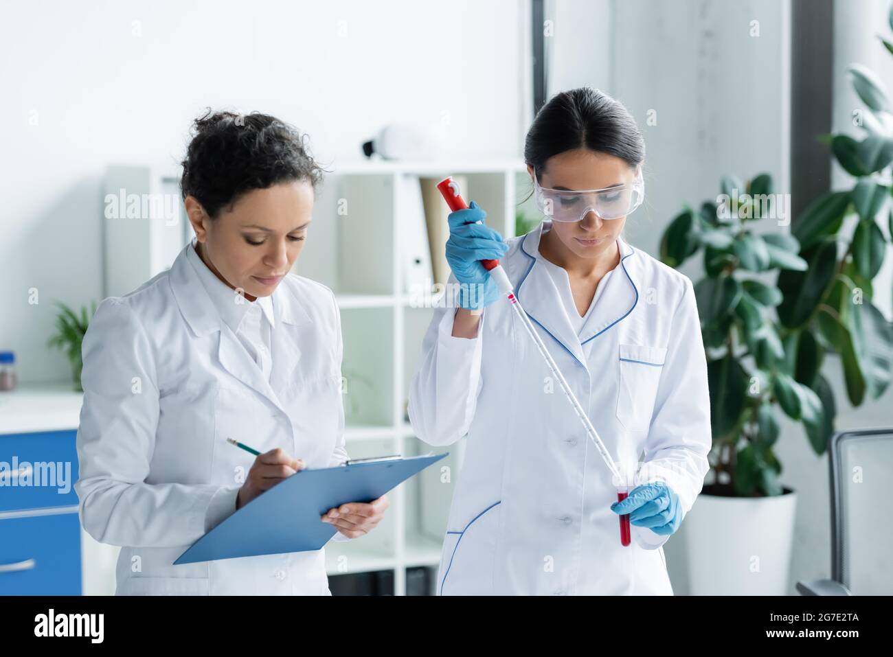 African american scientist writing on clipboard near colleague with ...
