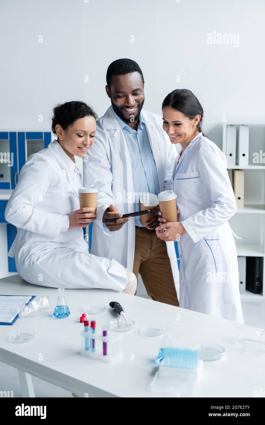 Positive interracial scientists with coffee looking at smartphone in ...