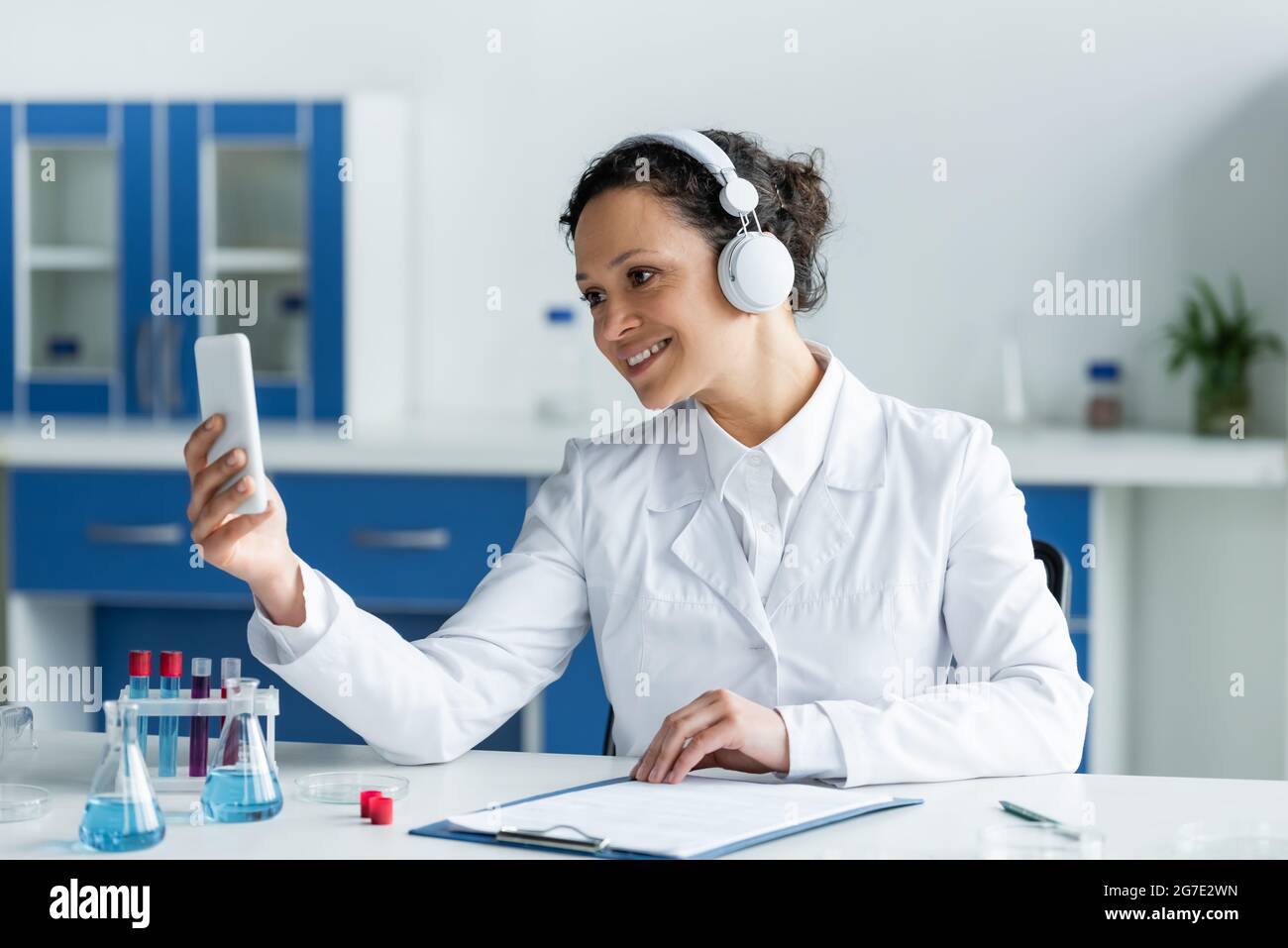 Smiling african american scientist in headphones holding smartphone ...