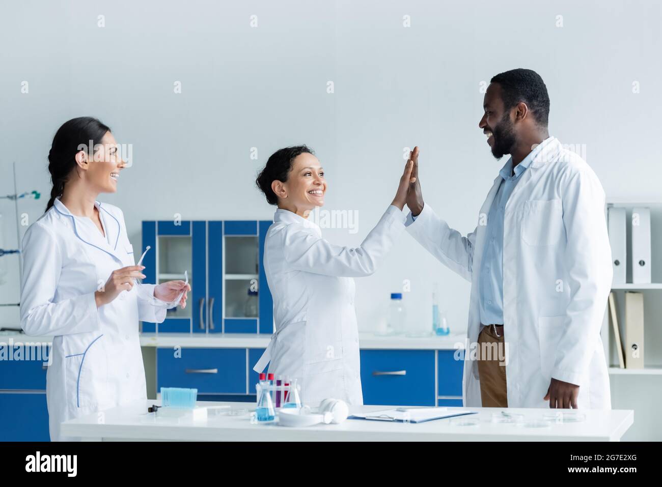 Smiling african american scientists giving high five near colleague ...