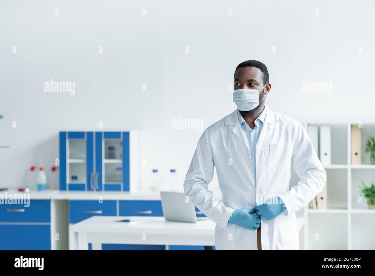 African american scientist in medical mask adjusting white coat in lab ...