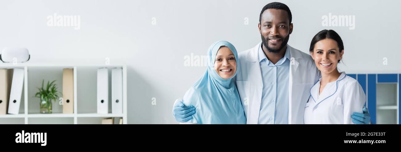 African american doctor hugging smiling colleagues in clinic, banner ...