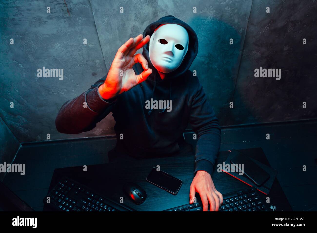 Anonymous hacker wearing face mask working on computer in dark room ...