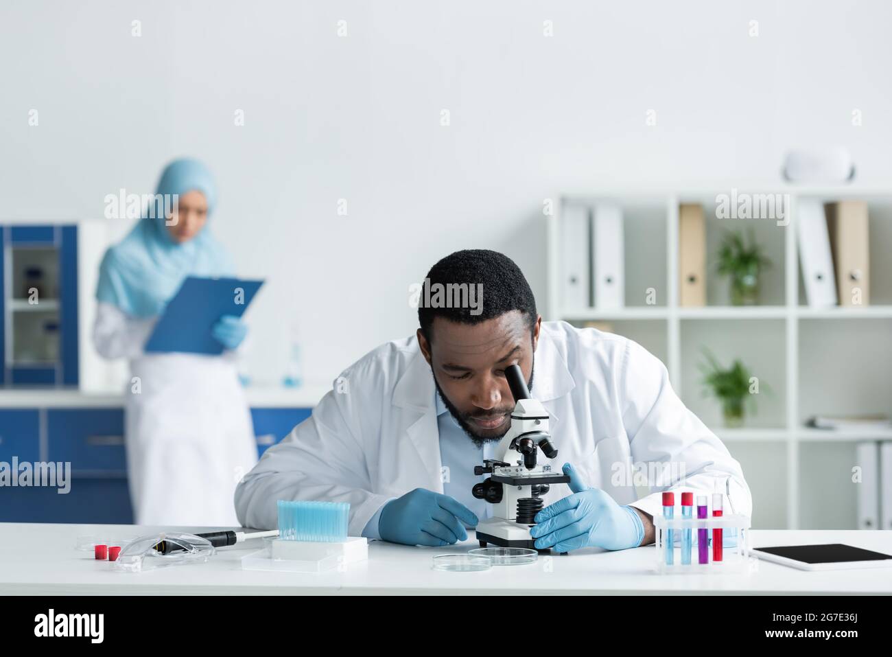 African american scientist in white coat looking through microscope ...