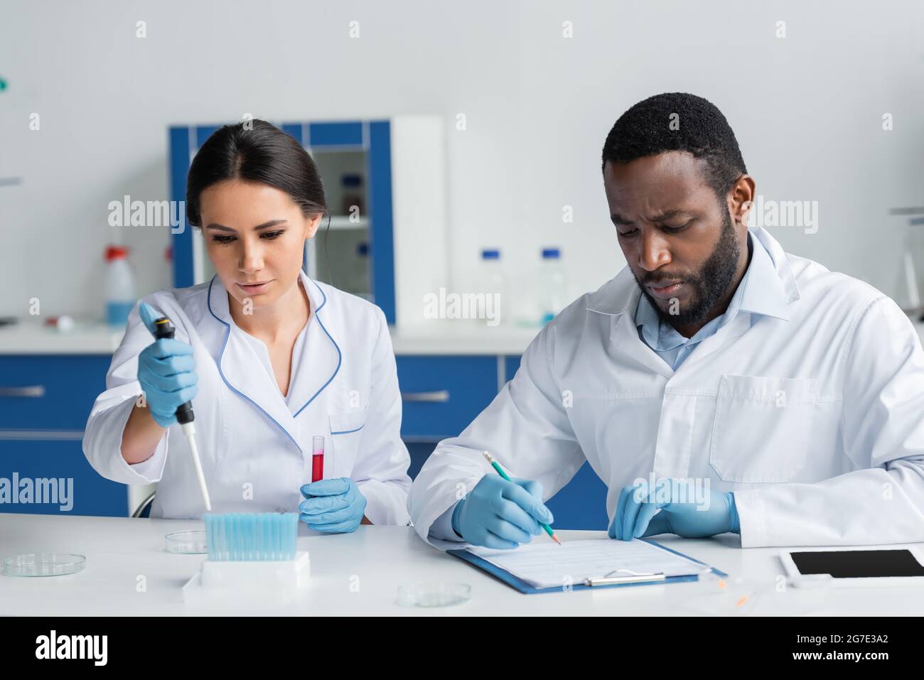 African american scientist writing on clipboard near colleague with ...