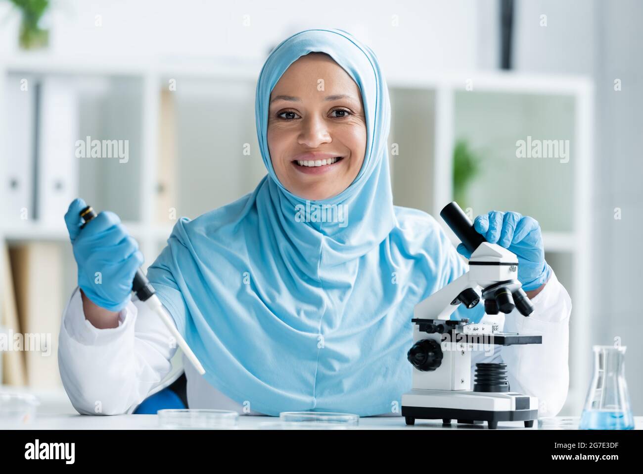Smiling arabian scientist holding pipette and microscope while working ...