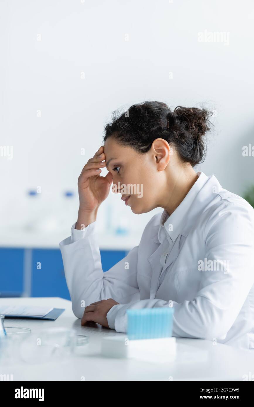 Side view of tired african american scientist sitting near medical ...