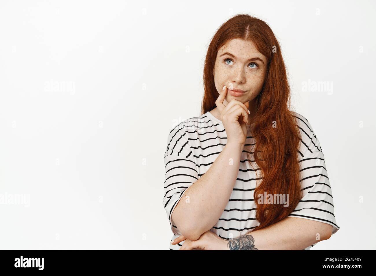 Thoughtful ginger girl looking up and thinking, making choice, staring ...