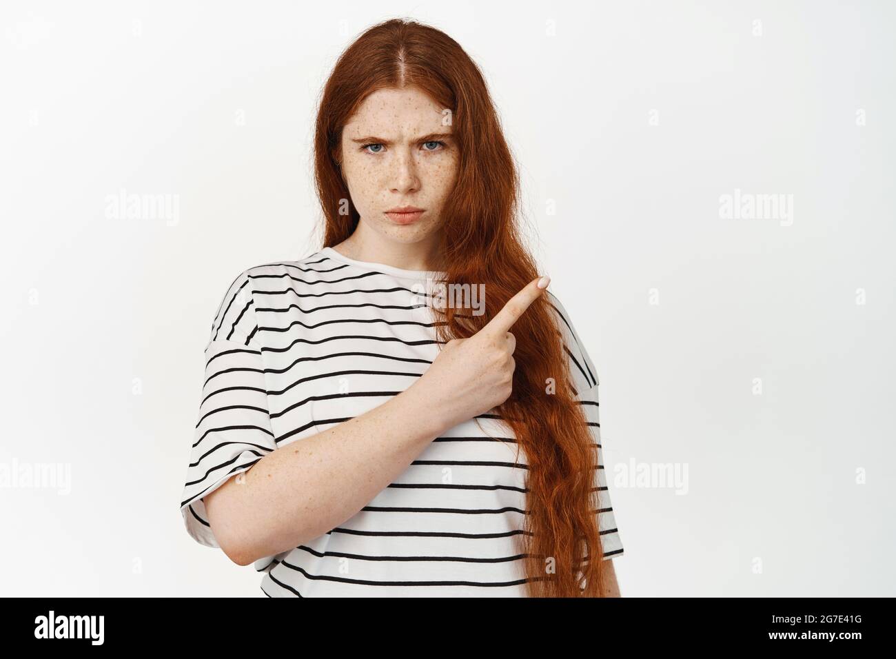 Upset young redhead girl complains, pointing right and frowning, look ...