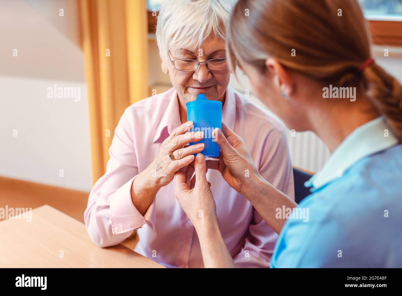 Caregiver helping senior woman drinking giving her a cup of water and ...