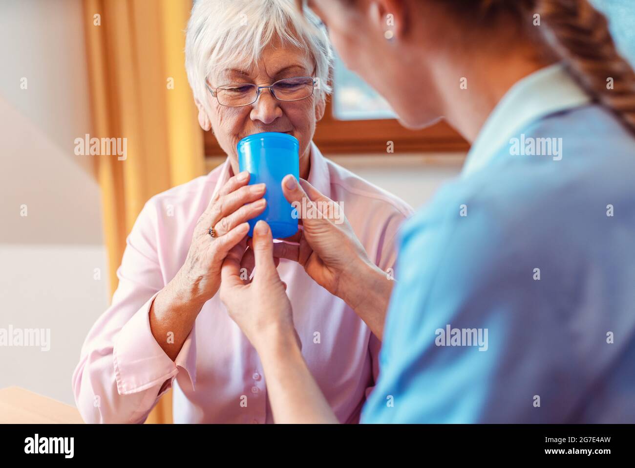 Caregiver helping senior woman drinking giving her a cup of water and ...