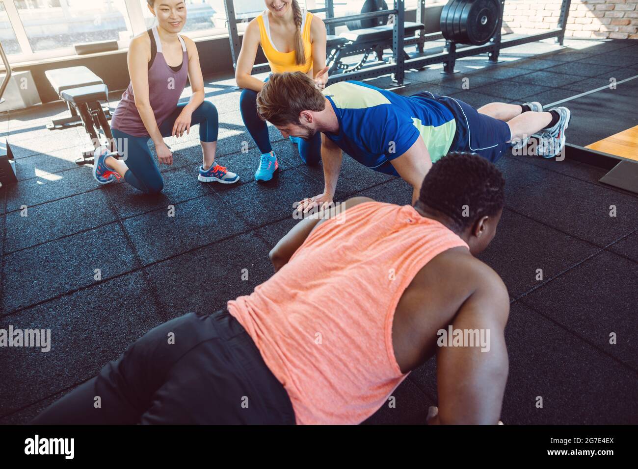 Two men have a push-up competition in the gym with girls cheering them ...