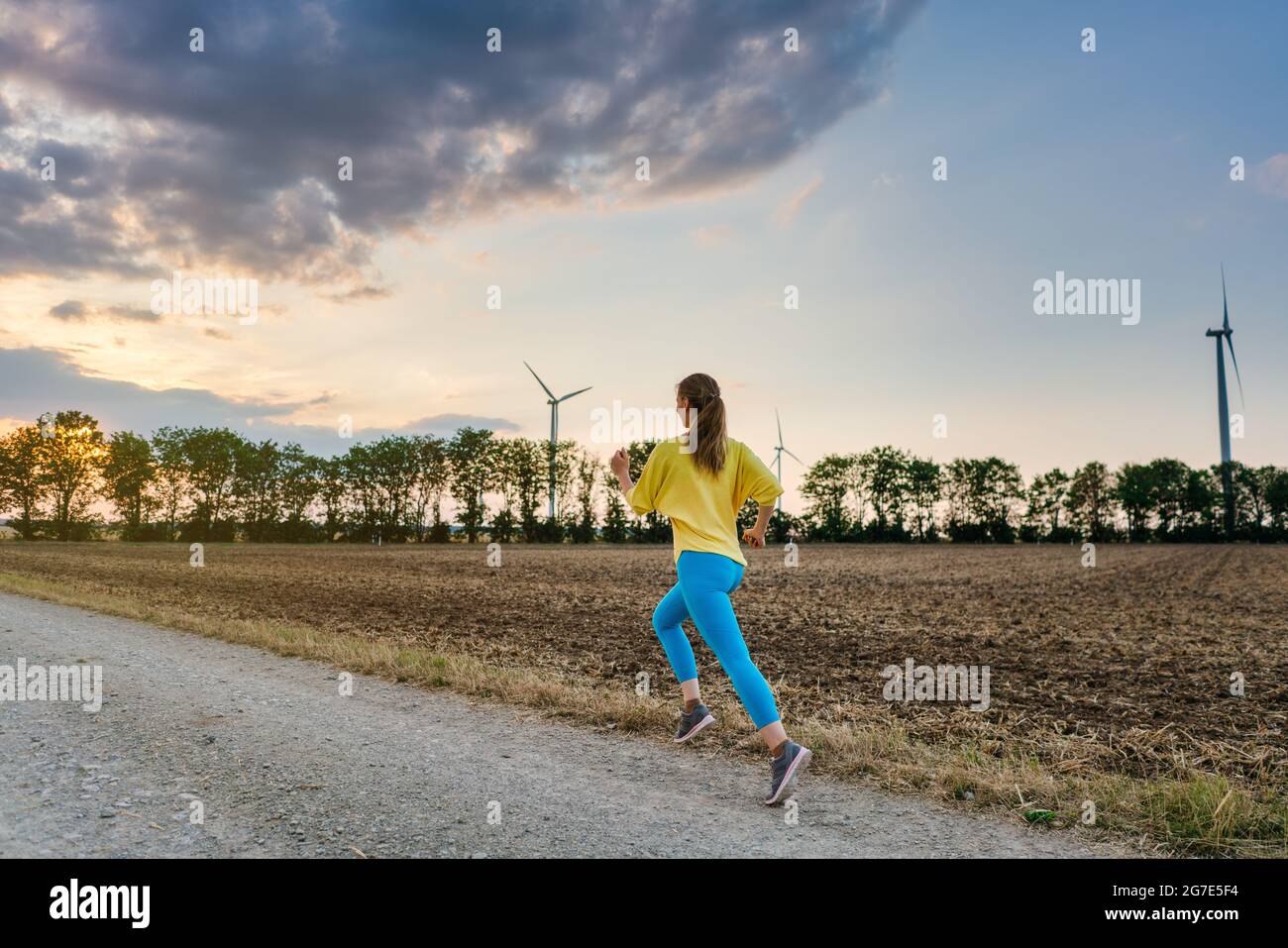 Woman running or jogging down a path in the countryside after sunset ...