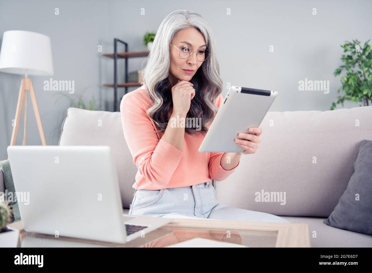 Photo of serious calm smart old woman look tablet wear glasses sit sofa ...