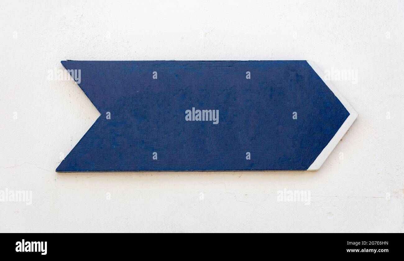 Signpost blue color wooden arrow on white wall. Blank direction label ...