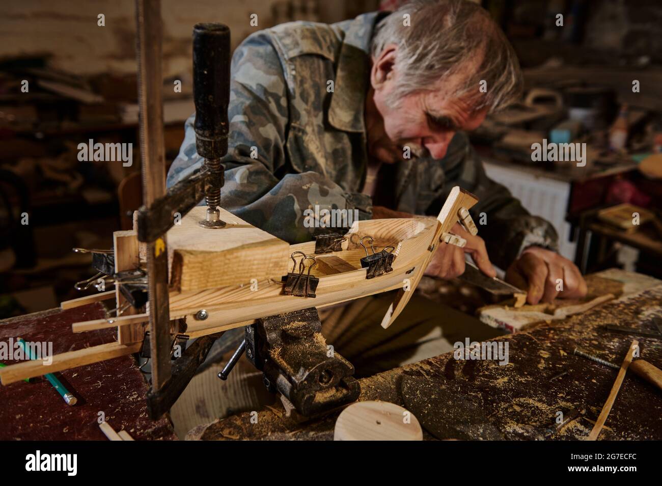 A mature carpenter works on a wooden toy sailboat in his workshop ...