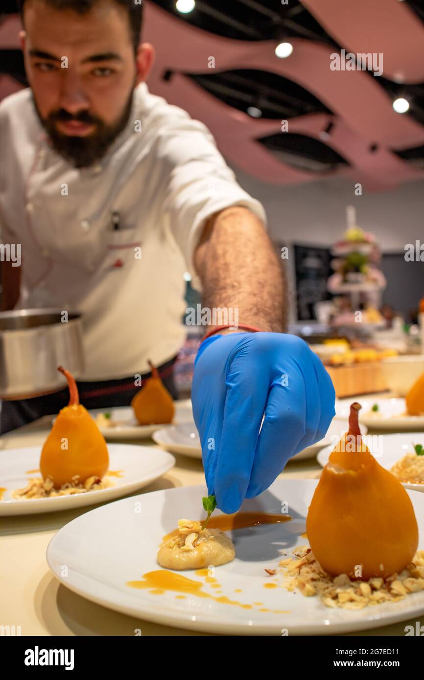 Kitchen chef decorating a plate with pears poached in orange wine and ...