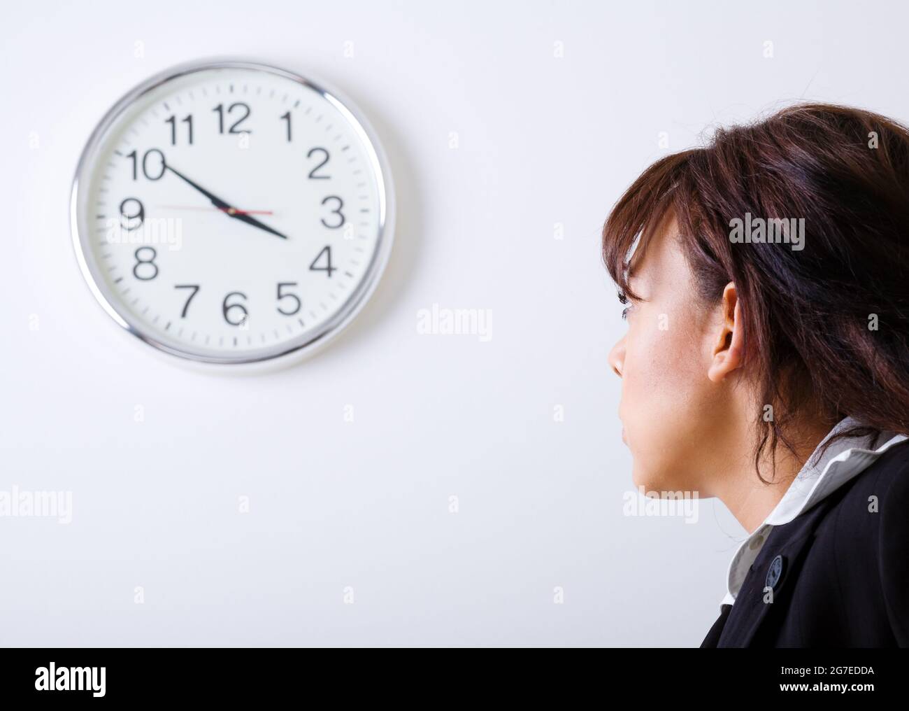 Female office worker looking at a clock on the wall Stock Photo - Alamy