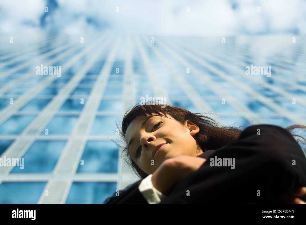 A young woman in a suit looking down to the viewer in front of a modern ...