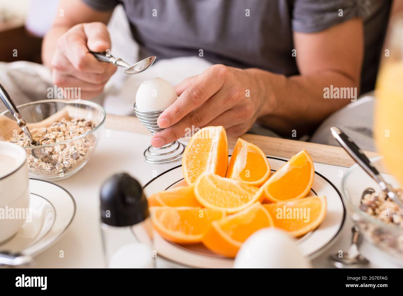 Man cracking open a boiled egg for breakfast using a spoon with cereal ...