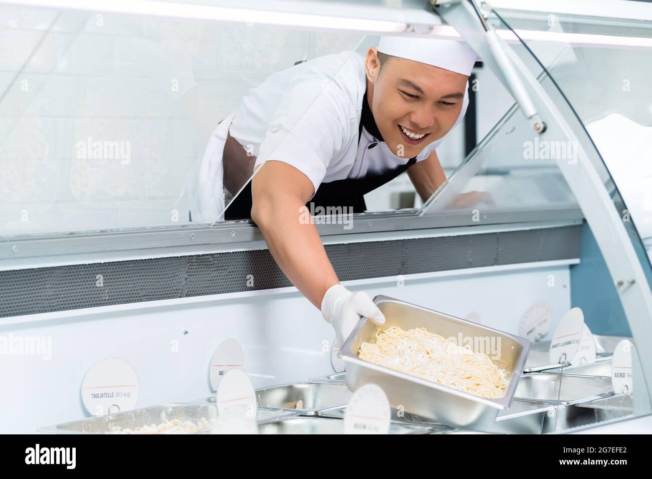 Smiling Asian chef filling a glass display counter with prepared food ...