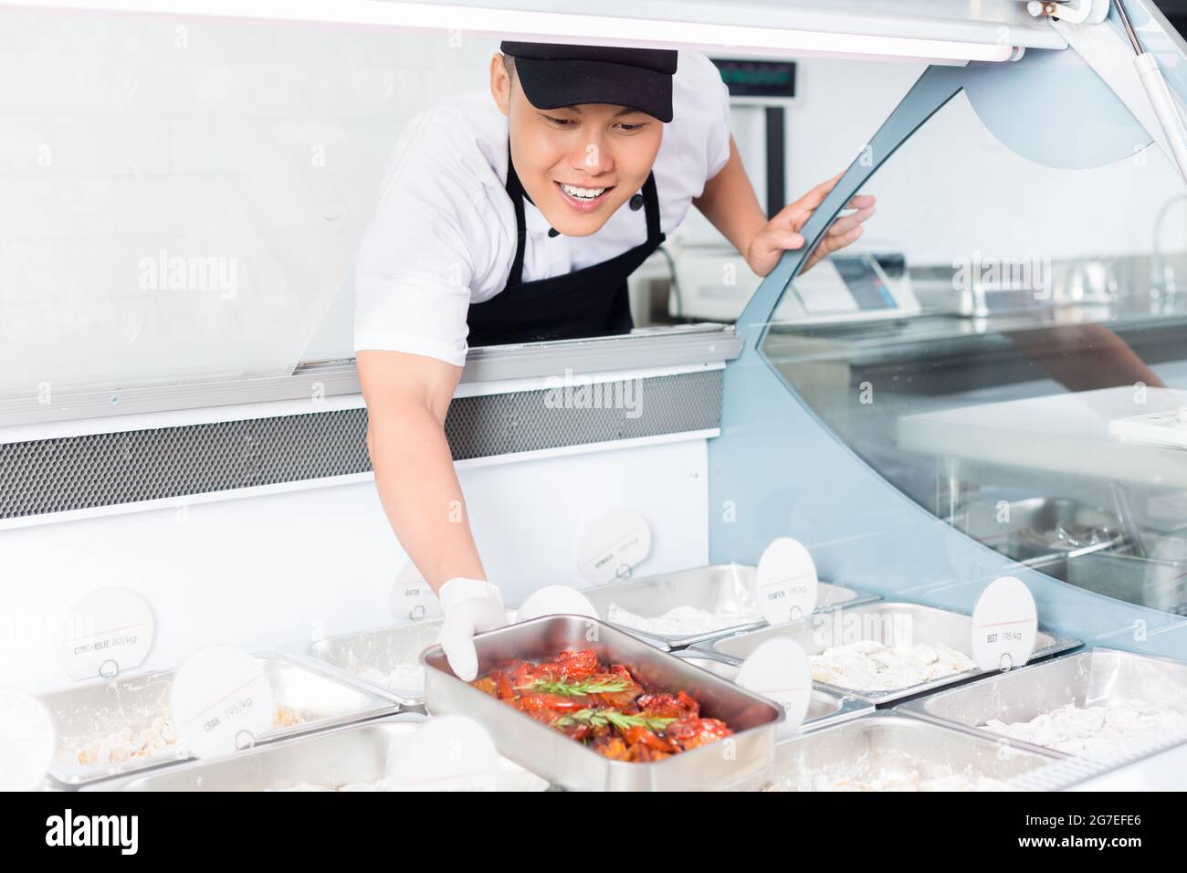 Chef replenishing a tray of food in a display in a delicatessen or ...