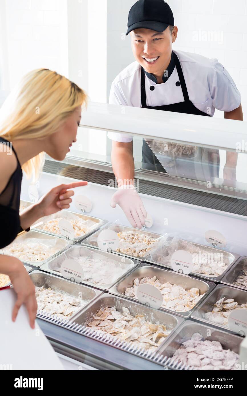 Smiling young Asian salesman presenting food to a female customer as ...