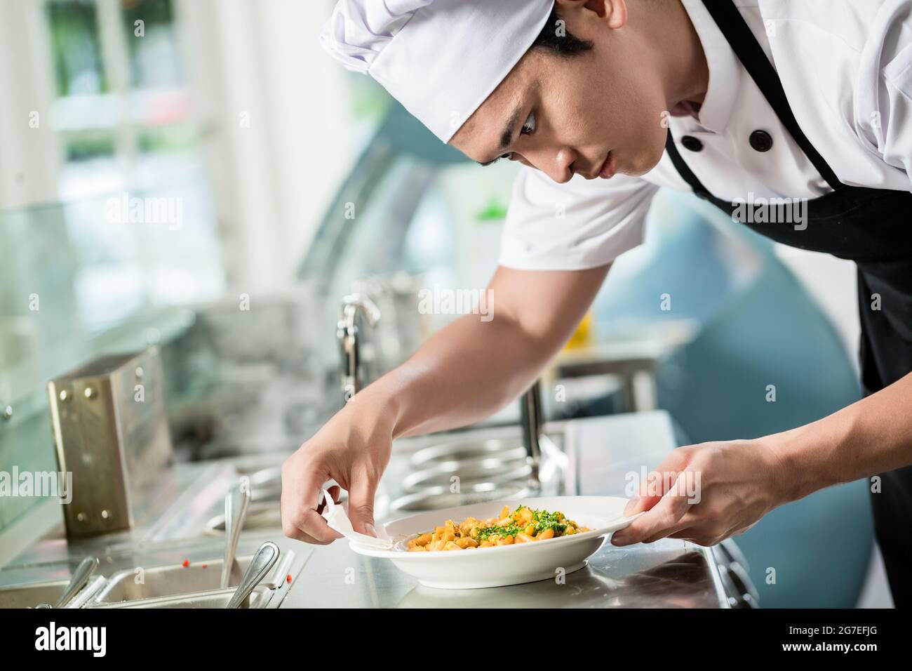 Gourmet chef plating up a dish of food in an Asian restaurant carefully ...