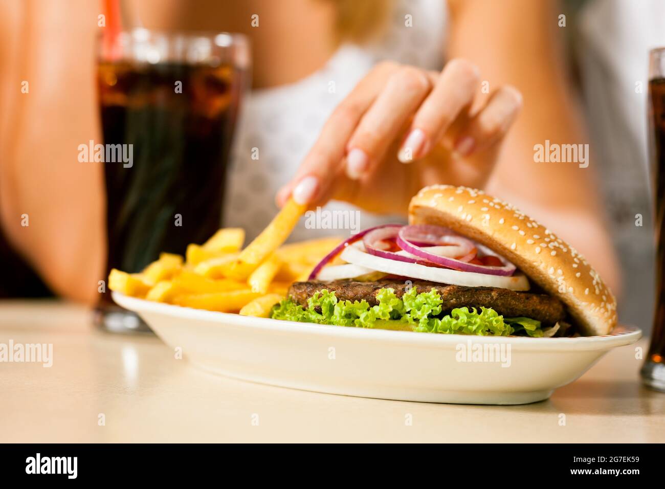 A woman eating hamburger and drinking soda in a fast food diner; focus ...