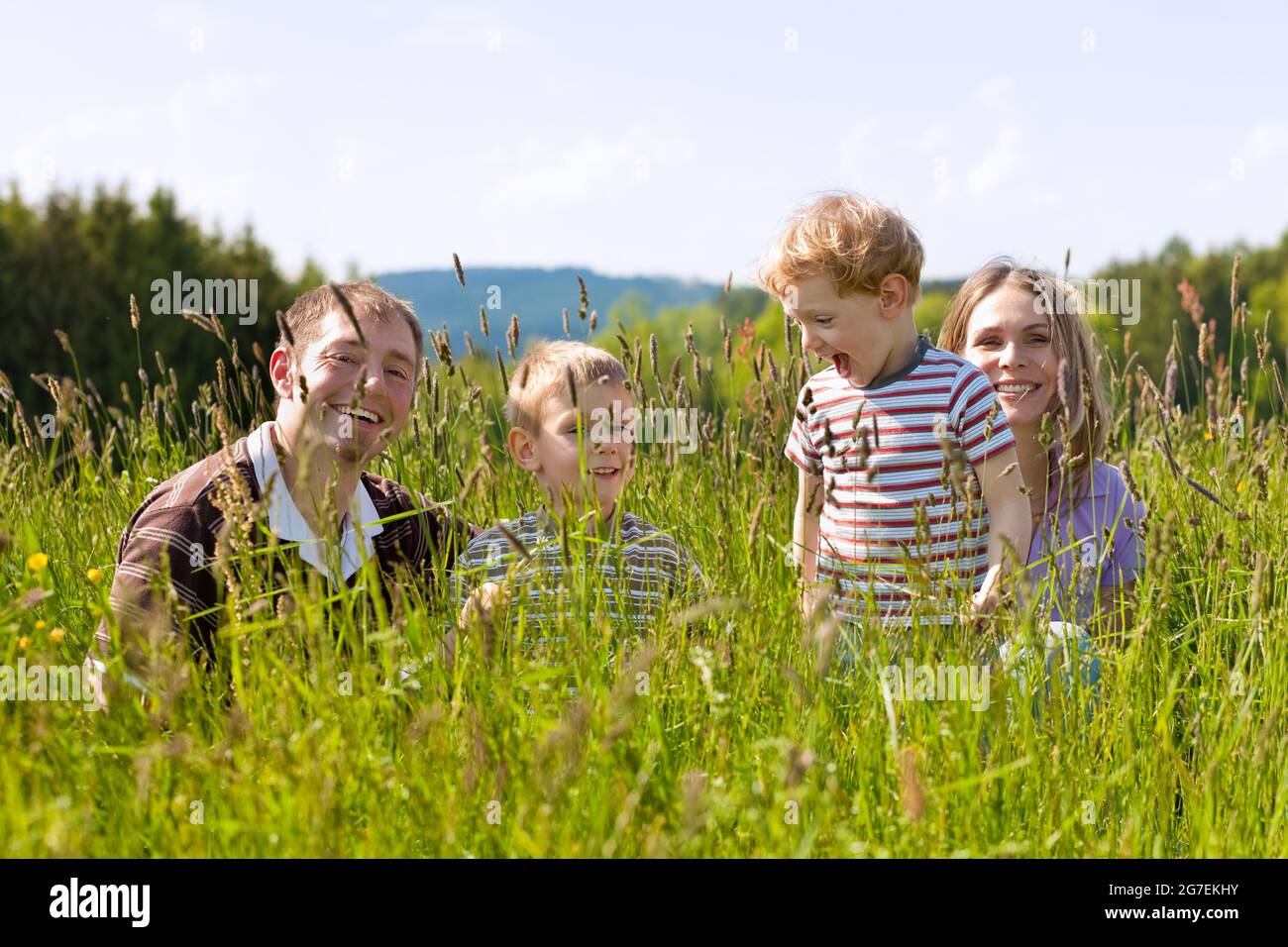 Very happy family with two kids sitting in a meadow in the summer sun ...