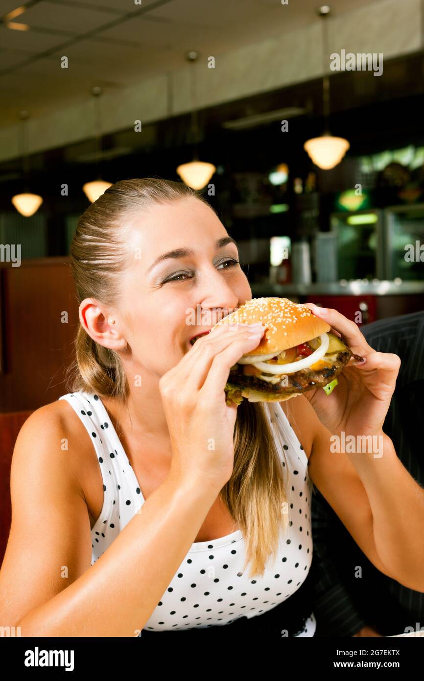 Happy woman in a fast food restaurant eating a hamburger and seems to ...