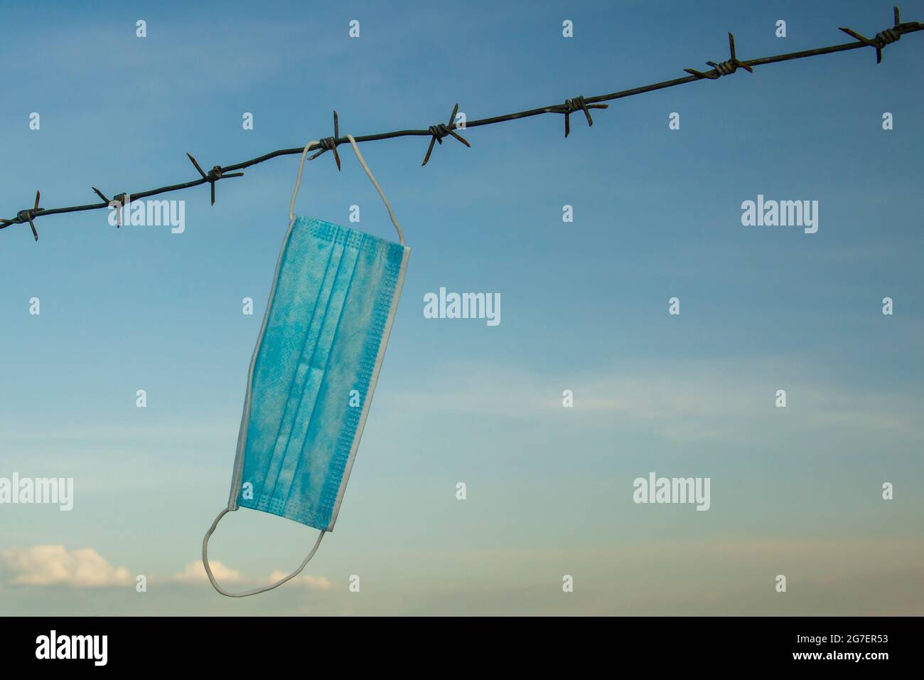 Medical surgical mask hanging on barbed wire against blue sky Stock ...