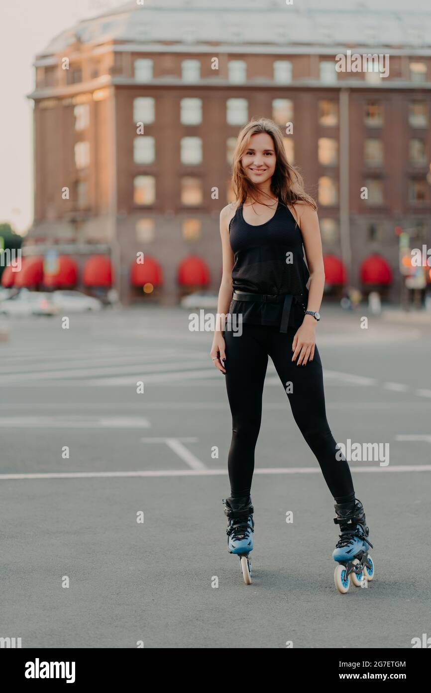 Vertical shot of healthy slim woman going rollerblading dressed in ...