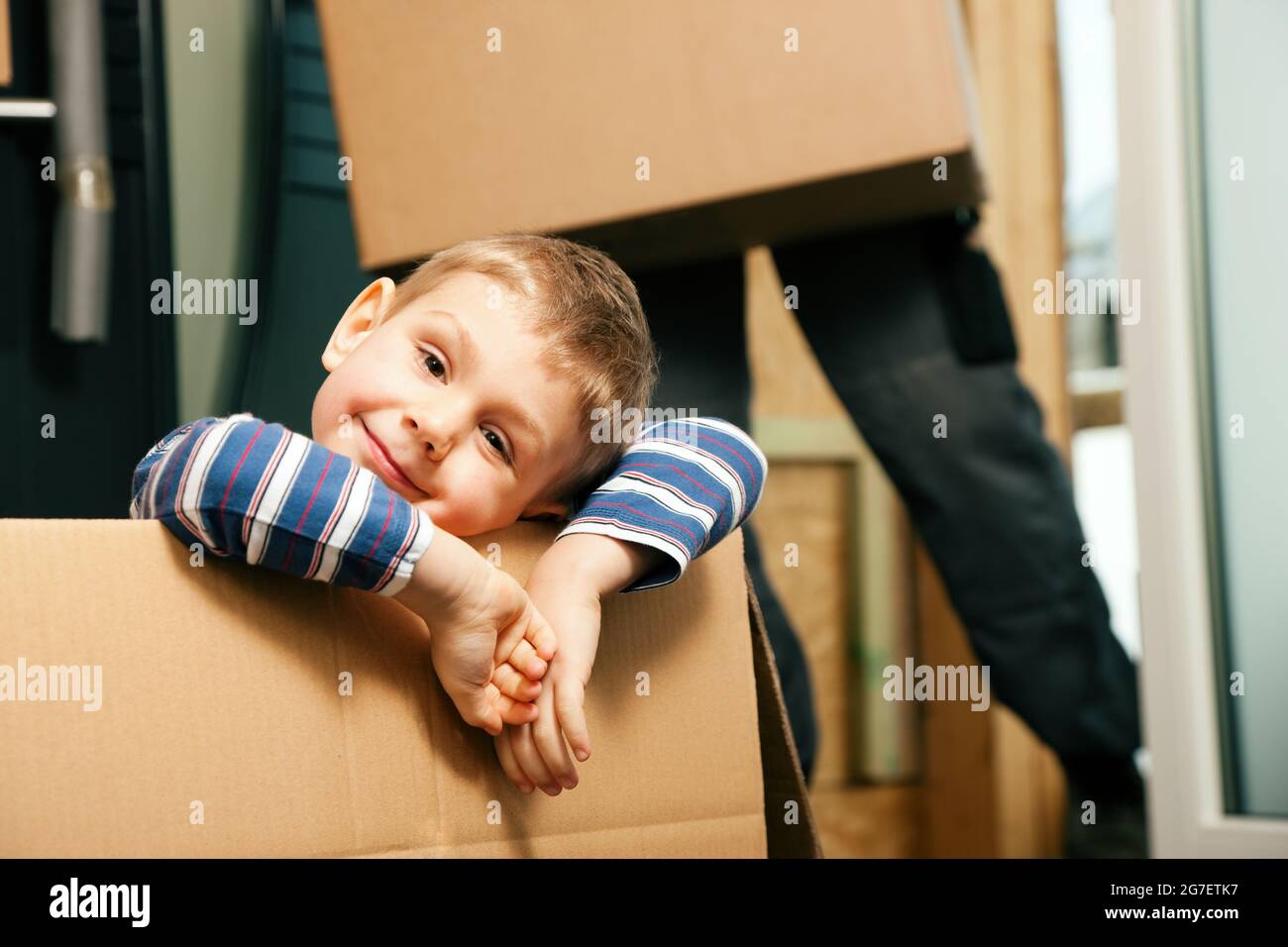 Family moving in their new home. The son is sitting inside a moving box ...