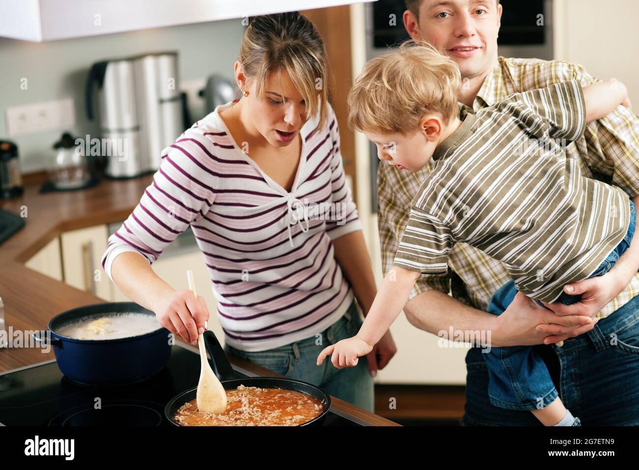 Family cooking in their kitchen - mother stirring some spaghetti sauce ...