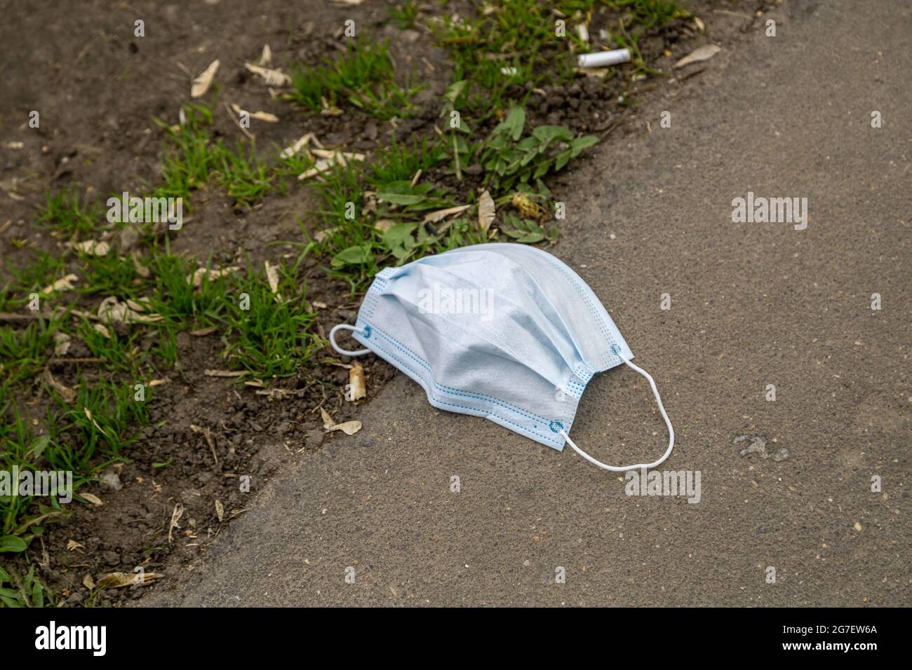 Used face mask on a wall next to green grass as environmental pollution ...