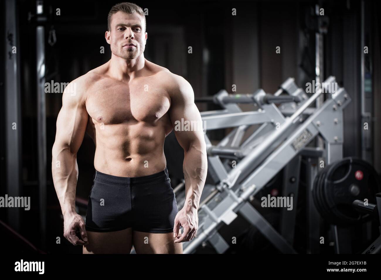 Strong man doing bodybuilding in gym standing in front of a dumbbell ...