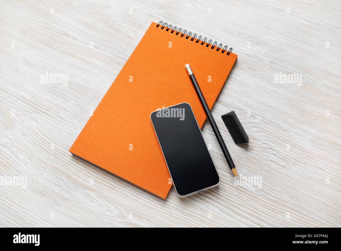 Blank orange notepad, smartphone, pencil and eraser on light wood table ...