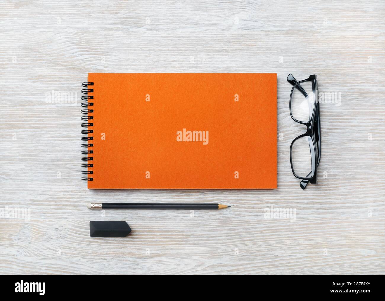 Orange notebook, glasses, pencil and eraser on light wood table ...