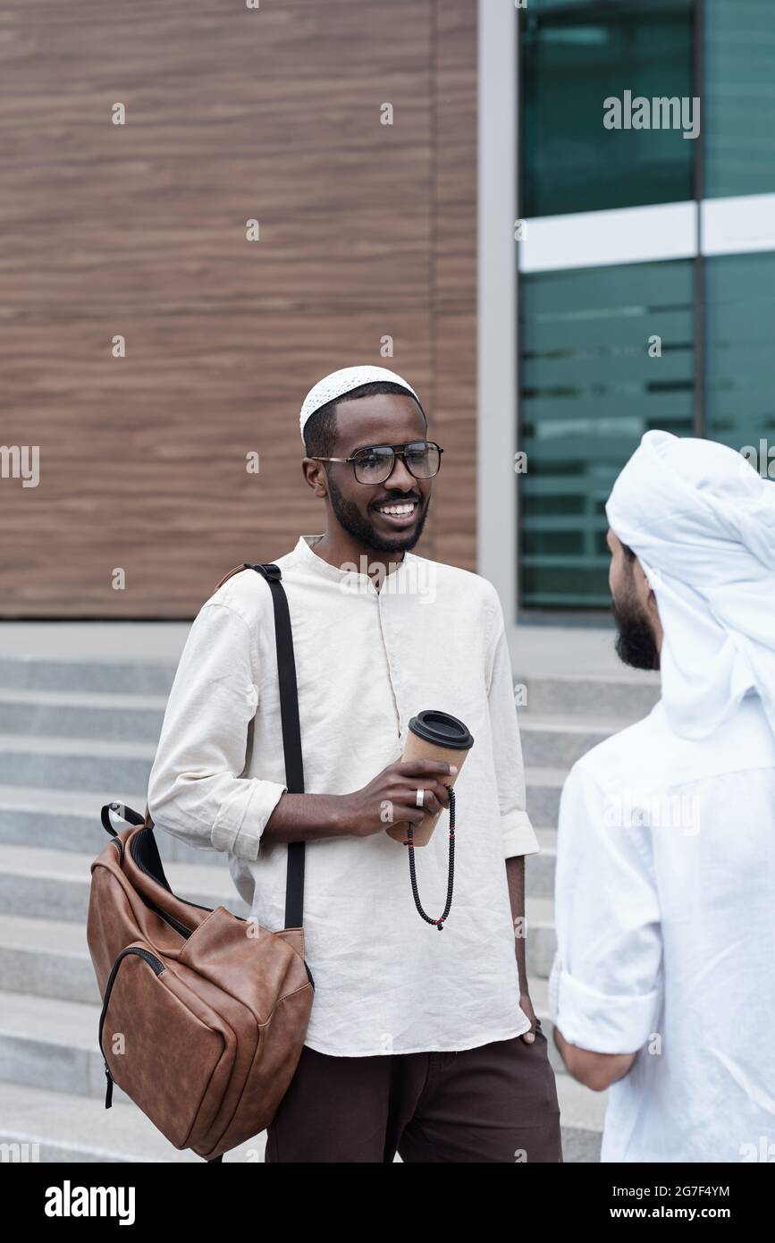 Positive young Muslim colleagues standing at stairs outdoors and ...
