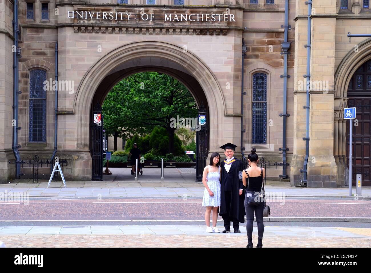 A male graduate in graduation costume and a friend pose for photo ...