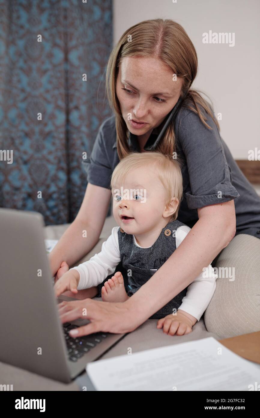 Curious blond-haired baby sitting in front of laptop while his multi ...