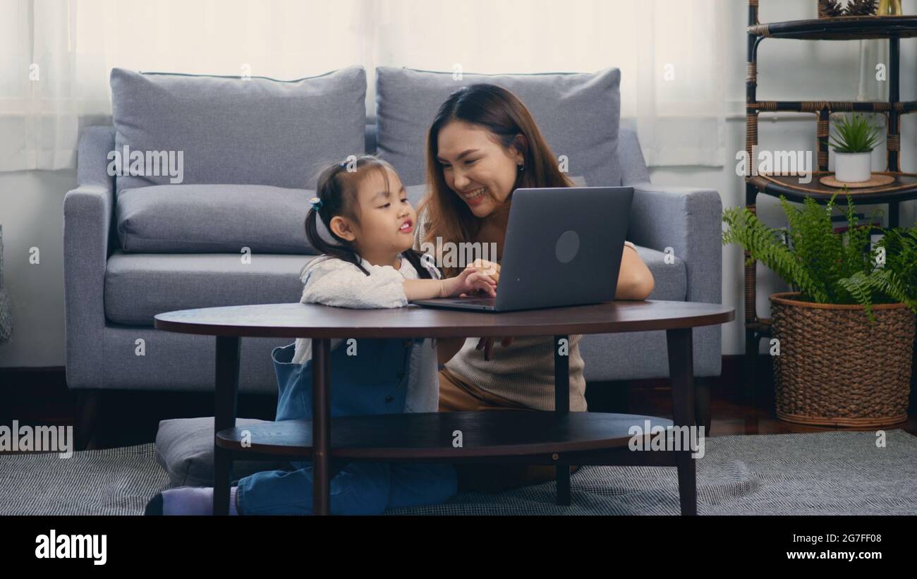 Asian young mother with laptop computer teaching her kid to learn or ...