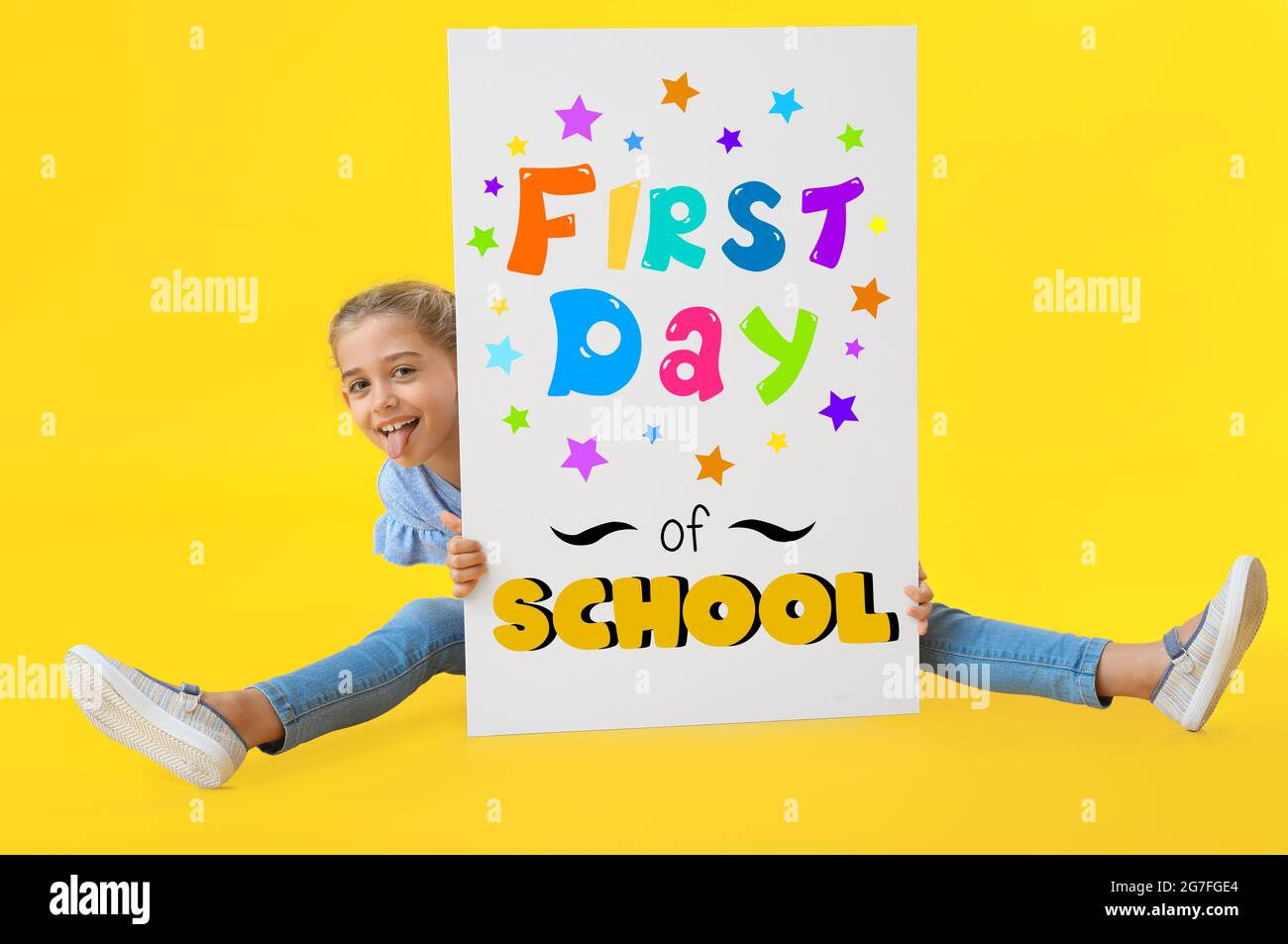 Funny little girl holding poster with text FIRST DAY OF SCHOOL on color ...